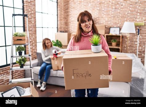 Mother And Daughter Moving To A New Home Holding Cardboard Box Clueless