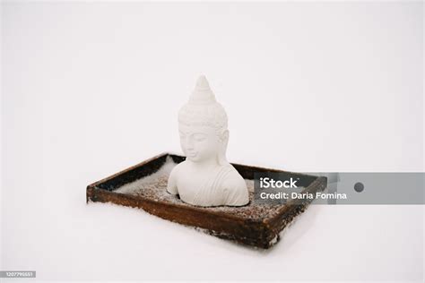 겨울에 눈이 내리는 동안 흰 눈으로 덮인 나무 스탠드에 석고로 만든 흰색 부처님의 작은 동상 0명에 대한 스톡 사진 및 기타
