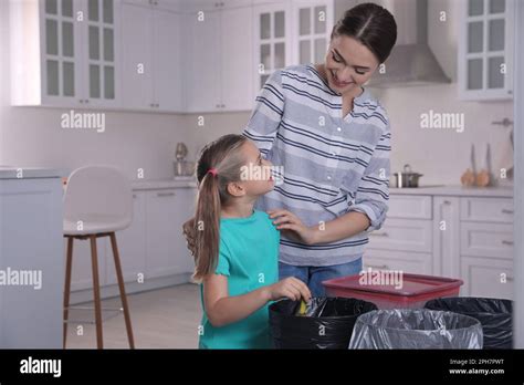 Young Woman And Her Daughter Throwing Banana Peel Into Trash Bin In
