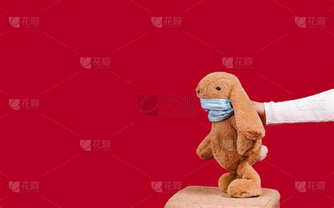 手拿传染病复活节兔子玩具，戴着医用口罩，望向空旷的空间。红色背景下的covid 19假日。卫生概