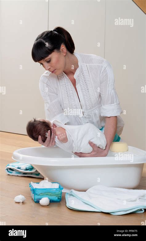 Baby Girl Swaddled In Muslin Cloth Being Lowered Into Bath To Prepare And Relax Her For Bathing