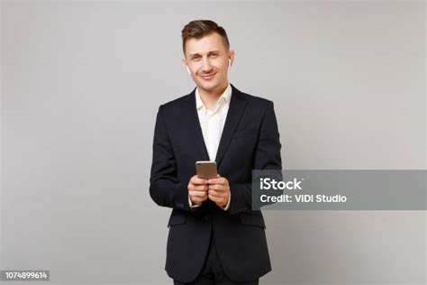 젊은 사업가 음악 휴대 전화를 사용 하 여 무선 이어폰 웃 고 회색 배경에 고립 Sms 메시지를 입력 성과 경력 부 비즈니스 개념입니다 복사 공간을 비웃는 다 검은색에 대한