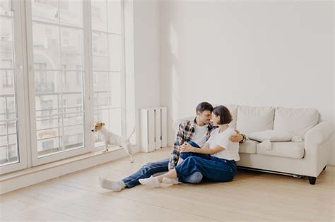 캐주얼 한 옷을 입고 행복한 애정 가족 부부의 수평보기 포옹과 서로 사랑을 표현 현대적인 아파트에서 소파 근처 바닥에 포즈