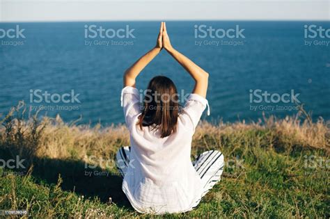 바다와 하늘을 볼 수있는 산 봉우리에 앉아 요가를하는 세련된 힙스터 소녀 요가와 명상을 연습 행복한 여자 텍스트의 공백입니다