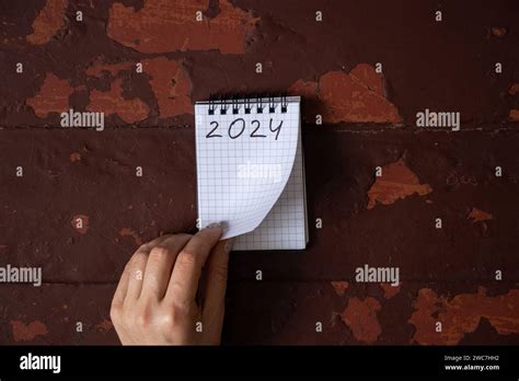 notepad with text 2024 and female hand turning page on wooden weathered