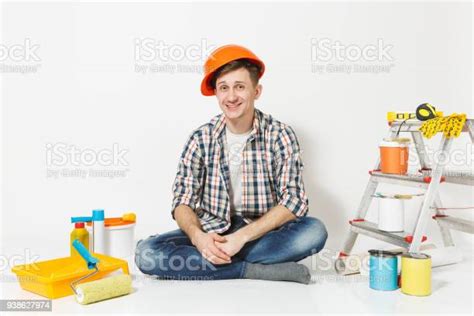재건축 아파트 룸 흰색 배경에 고립에 대 한 악기와 함께 바닥에 앉아 오렌지 보호 헬멧에 웃는 남자 배경 화면 액세서리 그림 도구를 붙이기입니다 수리 가정 개념입니다 개선에