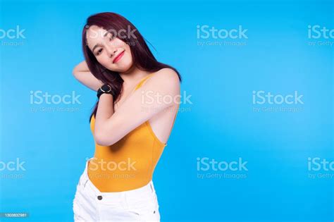 쾌활한 젊은 여성 갈색 긴 머리는 고립 된 파란색 배경에 서있는 동안 짧은 청바지를 착용합니다 카피 공간이있는 카메라를 보면서
