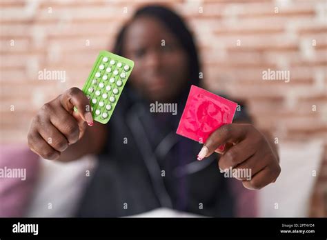 African American Woman Holding Condom And Birth Control Pills Sitting