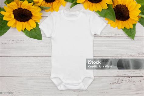 하얀 아기 소녀 또는 소년 보디 슈트 모형 플랫은 흰색 나무 배경에 해바라기와 함께 누워 있습니다 Oneie 템플릿 디자인 인쇄