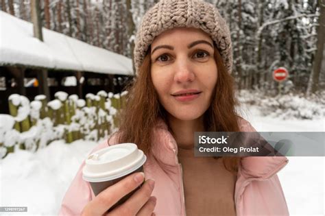 검은 종이 커피 컵을 들고 부드럽게 웃고 카페에 혼자 서서 손에 커피를 마시고 기분이 좋은 기분을 가진 것을 기쁘게 생각합니다 창 뒤의 겨울 갈색 머리에 대한 스톡 사진 및