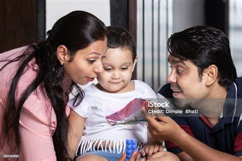 여러 가지 빛깔의 블록을 가지고 노는 귀여운 어린 딸과 함께 행복한 장난기 많은 인도 부모 어린 소녀 아이와 어머니에게 붉은 색 조각을 보여주는 아버지는 실내에서 함께