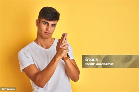 고립 된 노란색 배경 위에 서있는 흰색 티셔츠를 입은 젊은 인도 남자손 제스처로 상징적 인 총을 들고 살인 사격 무기 화가 난 얼굴 T 셔츠에 대한 스톡 사진 및 기타