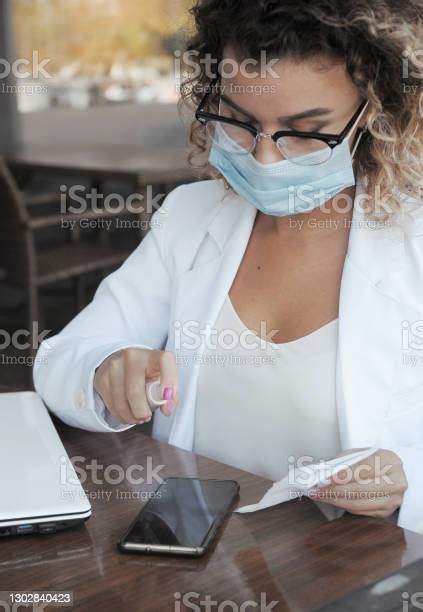얼굴에 마스크를 가진 아름다운 여자는 야외에서 노트북을 작동하기 전에 그녀의 손을 살균합니다 거리 작업 20 24세에 대한 스톡