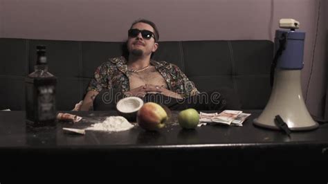 Rich Drug Dealer Man Yawns Sitting On Sofa Near Table With Cocain Stock