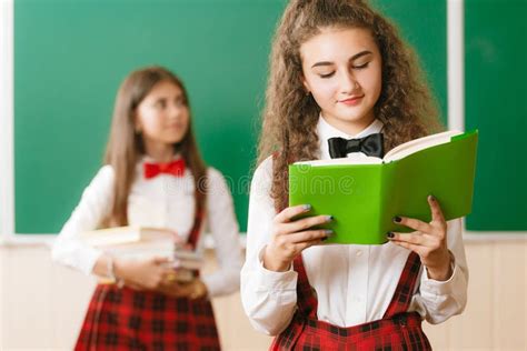 2 милых школьницы в стойке школьной формы с книгами в классе на фоне классн классного Стоковое