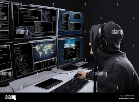 Rear View Of A Hacker Using Multiple Computers For Stealing Data In