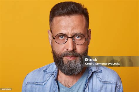 데님 재킷과 둥근 스페이클을 입고 노란색 배경에 서있는 동안 남성잘 생긴 중년 수염 남자의 초상화를 닫습니다 사람 개념 근육질