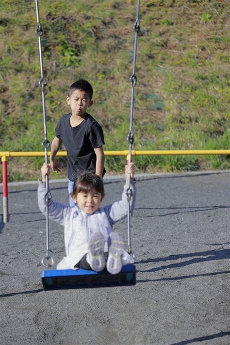 Japanese Sister On The Swing And Brother Pushing Her Back Stock Image
