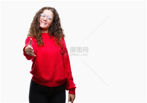 美丽的黑发卷年轻女孩戴着眼镜和冬季毛衣在孤立的背景微笑友好地提供握手作为问候和欢迎高清图片下载 正版图片505841287 摄图网