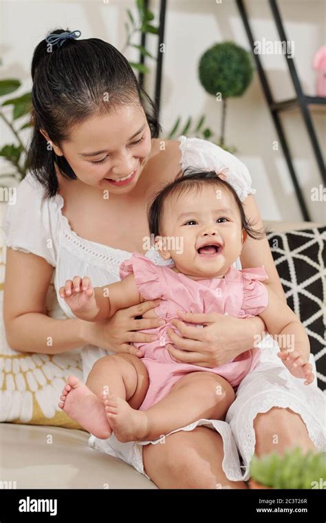 Smiling Pretty Young Asian Woman Sitting On Couch And Tickling Her