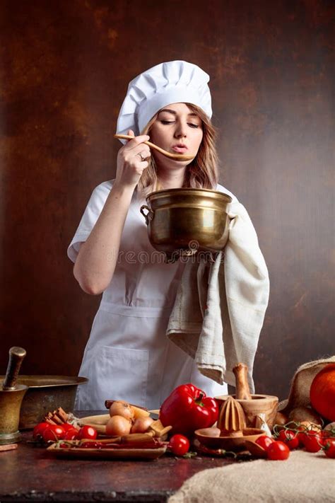 Young Woman In A Chef Uniform With Old Brass Pan And Wooden Spoon Stock