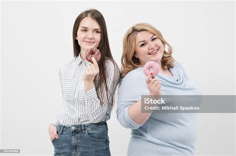 두 여자 얇은 흰색 배경에 지방 그들의 손에 분홍색 유약 도넛을 들고 있다 2명에 대한 스톡 사진 및 기타 이미지 2명