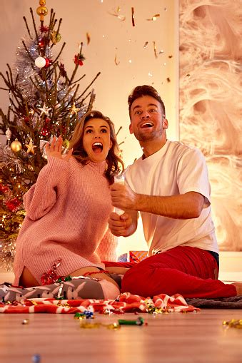 사랑에 빠진 젊은 커플은 크리스마스 트리 근처 바닥에 앉아 새해 크래커를 불고 색종이 조각으로 불꽃놀이를 감상합니다 크리스마스와 새해를 준비하고 즐기는 아름다운 연인들 12