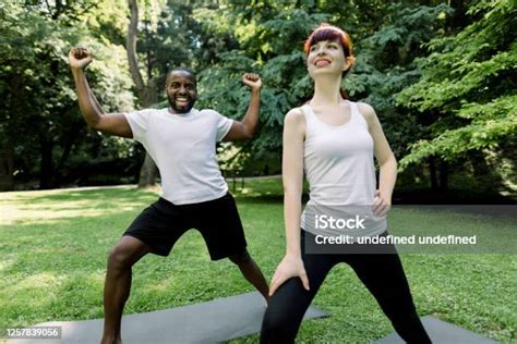 다른 운동을하는 매트에 서 다민족 피트니스 사람들 야외 에서 운동에 미소와 백인 예쁜 여자 미소 짓는 아프리카 남자에 초점 은 뒤에 서 자신의 주먹을 유지 2명에 대한 스톡