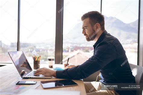 Side View Of A Caucasian Businessman Working In A Modern Office Sitting At A Desk By A Window
