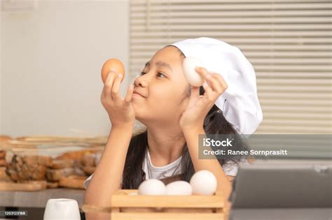 흰색 요리사 모자를 쓰고 있는 어린 아시아 소녀가 오리 달걀과 치킨 에그를 들고 빵집을 만들고 있습니다 8 9 살에 대한 스톡