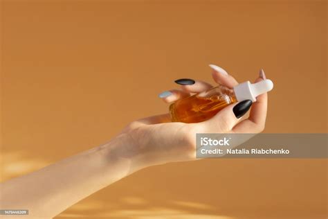 여자의 손은 갈색 배경에 스포이드 캡이 있는 유리병을 들고 있다 얼굴에 오렌지 세럼으로 라벨이없는 병 화장품 피부 관리와