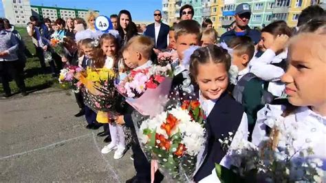 Девочки с бантами и в белоснежной форме мальчишки в костюмах и у всех в руках цветы классика