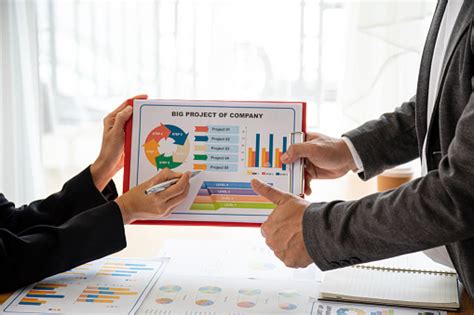 회의 중에 프로젝트 차트와 그래프에 대해 논의하고 회사 프로젝트 세부 정보 팀워크 협업 및 데이터 분석 개념이 포함된 차트에 중점을 두는 비즈니스 전문가 2명에 대한 스톡