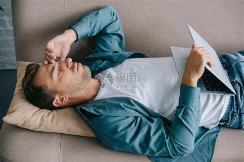 躺在沙发上头疼的年轻人拿着笔记本电脑高清图片下载 正版图片503487267 摄图网