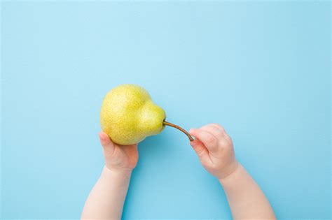 배를 들고 아기 손 밝은 파란색 테이블 배경에 신선한 과일입니다 파스텔 색상입니다 근접 촬영 시점 샷 하향하 보기 아이에 대한