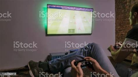 비디오 게임을 재생 하는 두 남자 콘솔 컨트롤러를 들고 손 텔레비전에 축구 또는 축구 게임 벽에 와이드 스크린 Tv 걸림 비디오