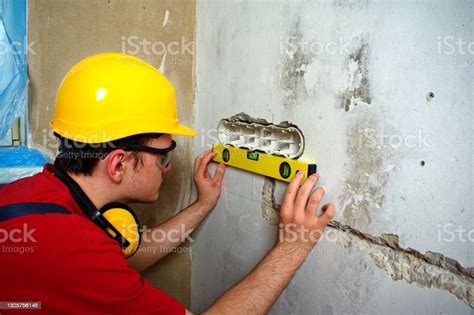 소켓에 대한 플라스틱 상자에 시도 가운을 입은 젊은 노동자 건설 헬멧 레벨이 있는 보호 헤드폰 전기 수리 및 배선 개념 20 24세에 대한 스톡 사진 및 기타 이미지