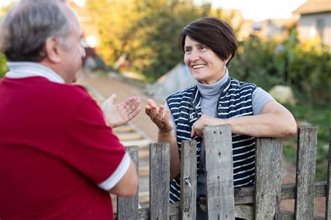 Neighbors Standing At Fence Outdoors And Having Conversation Village