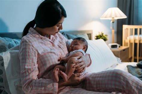 Premium Photo Loving Asian Mother Sitting On Bed In Pajamas Is