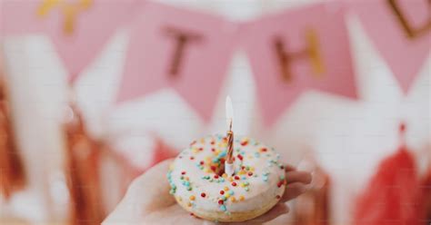 생일 축하해요 분홍색 화환과 방의 장식을 배경으로 촛불이 있는 맛있는 생일 도넛을 들고 있습니다 생일 파티 축하 스프링클이