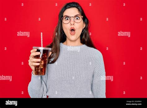 Young Beautiful Girl Wearing Glasses Drinking Sweet Drink Soda Over Red