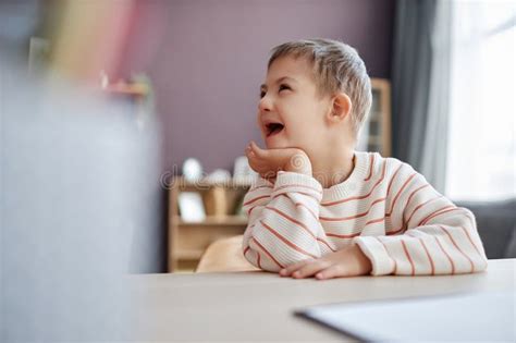 Menino Feliz Síndrome De Down Sentado Em Uma Mesa Na Escola E Rindo Foto de Stock Imagem