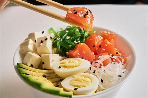 여자 손에 들고 젓가락 연어 아보카도 밥 그릇을 찌를 華 샐러드 치즈 메 추 라 기 계란 흰색 배경 쪽 보기에 고립 된 흰색과