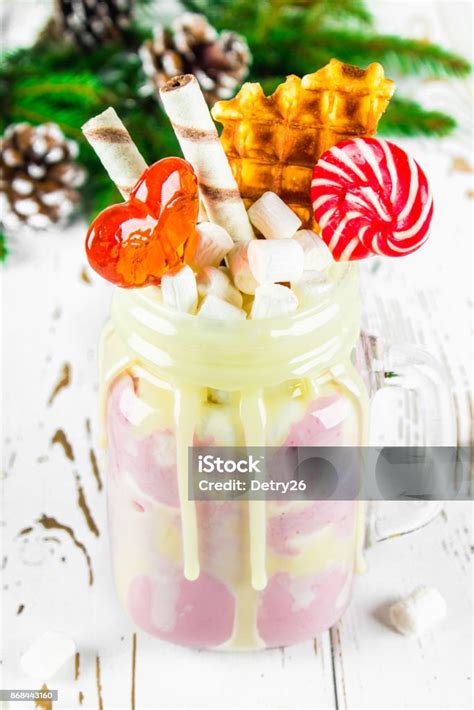 Freakshake 핑크 스무디 크림 막대 사탕 와플 마 시 멜로와 Monstershake입니다 메이슨 단지에 있는 극단적인 밀크 쉐이크 흰색 나무 테이블입니다 분위기가 새