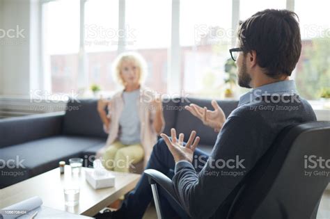 후면 유리 아늑한 사무실에 치료에 환자의 정신 상태를 주석 하면서 안락의 자 및 몸짓 손에 앉아 심각한 심리학자의 보기 건강관리와 의술에 대한 스톡 사진 및 기타 이미지