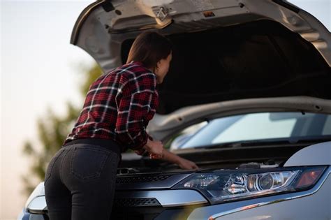 Una Mujer Mirando Dentro De Un Auto Con El Capó Abierto Foto Premium