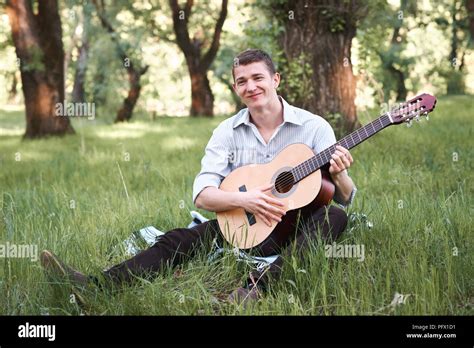 Young Man Playing Guitar In The Forest Sit On The Grass Summer Nature