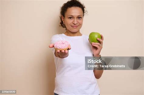 신선한 녹색 사과와 뿌려진 분홍색 도넛을 들고 있는 여성은 건강에 좋은 음식과 단 음식 사이의 선택을 나타냅니다 40 44세에 대한 스톡 사진 및 기타 이미지 Istock