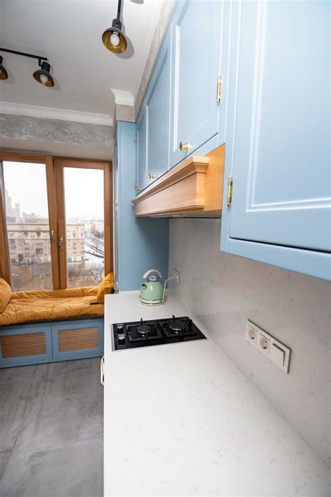 Малая кухня с навесным порталом и лежанкой у окна в древесном и небесно голубом декоре John Green