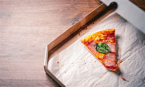 모짜렐라 치즈 햄 베이컨 토마토 소스 후추 향신료 바질을 곁들인 피자 한 조각 나무 테이블 배경에 골판지 상자에 이탈리아어 피자